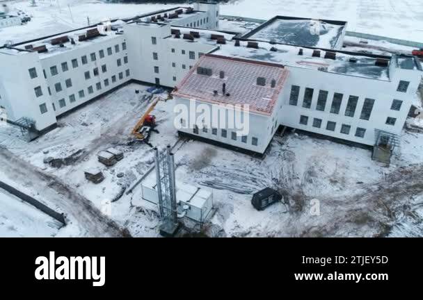 Crane with safety cradle near large school building on winter day aerial view. Facade repair ...