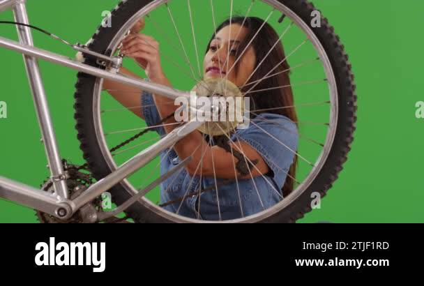 Young Latina woman struggling to fix her bike tire on green screen. On ...