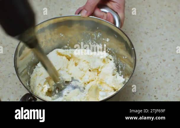 A close-up of a housewifes hands stirring the curd dough with a hand ...