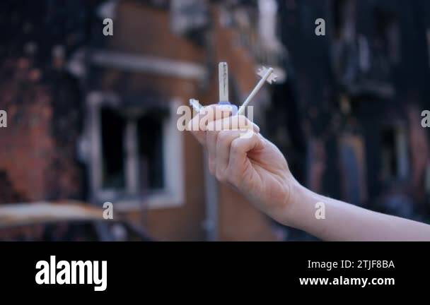 Close-up house keys in female hand at background of ruined building ...