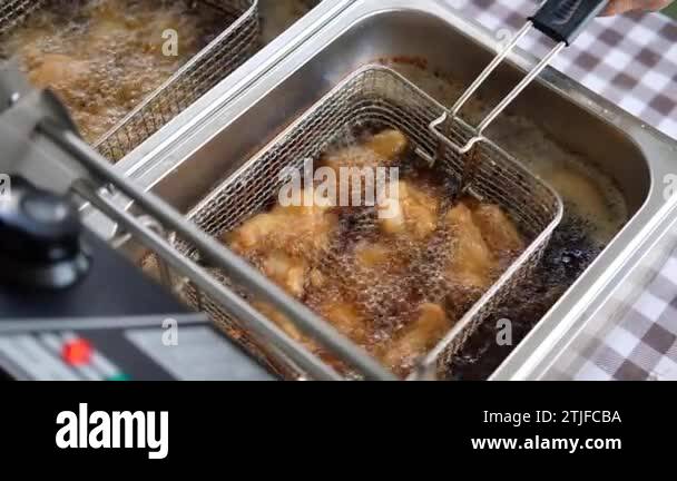 Frying chicken in deep fryer with bubbles of the oil are boiling while ...