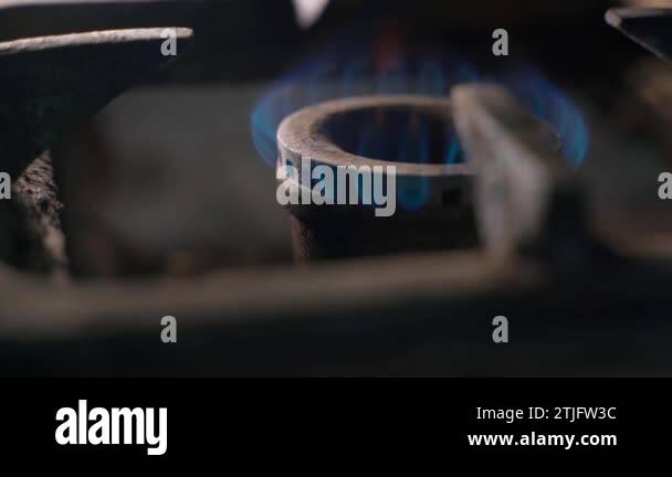 Blue fuel burns in the burner of an old untidy kitchen stove close-up ...