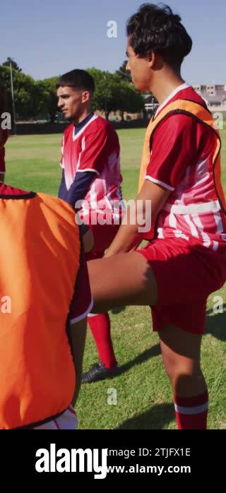 Vertical video of diverse group of male football on field streching ...