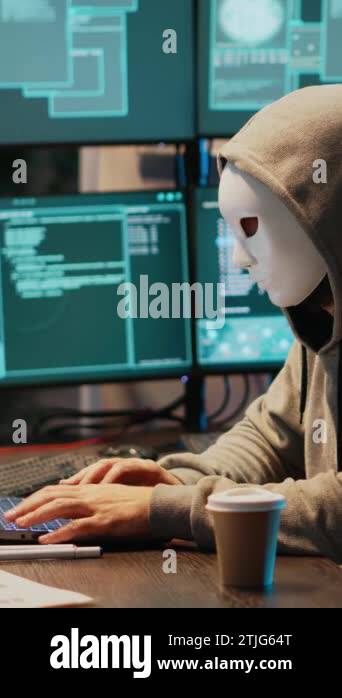 Vertical video: Cyber terrorist with mask hacking database servers, hacker with hood on hacking ...