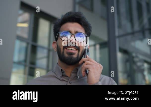 Happy Arabian businessman talk mobile phone in city near business office building smiling Indian ...