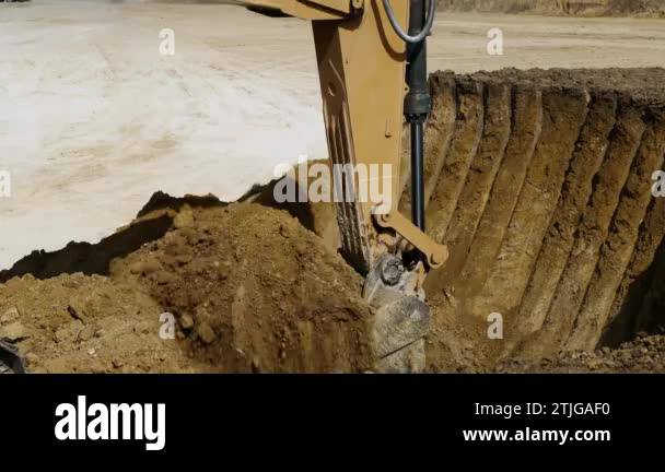 Yellow crawler excavator in the quarry picks up a pile of sandy soil in ...