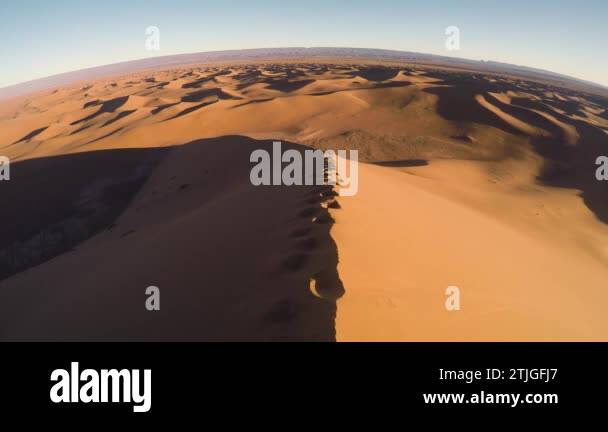 A person traverses a colossal sand dune, their footsteps etching a ...