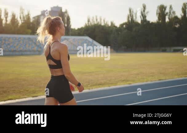 Blonde, walking on a running track in stadium, performing breathing ...