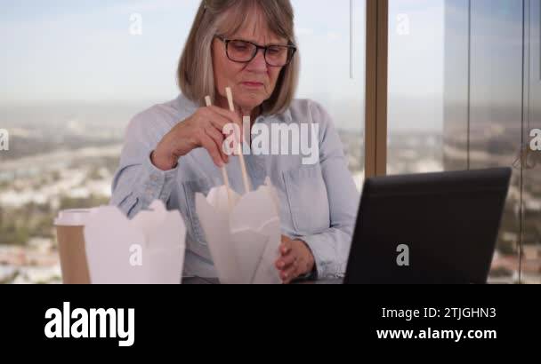 Senior professional woman on lunch break eating and using laptop in ...