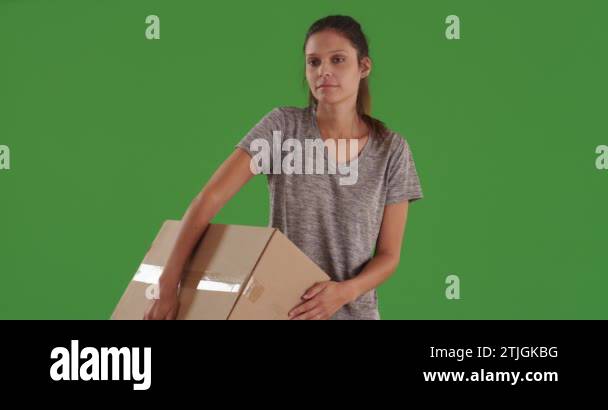 Somber young white girl carrying cardboard box for shipping on green ...