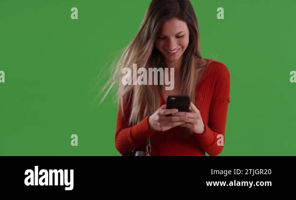 Millennial woman text messaging on her smartphone while smiling and laughing as wind blows her ...