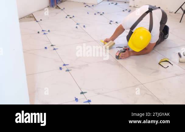 Professional laying of ceramic tiles on a concrete floor. The worker is ...