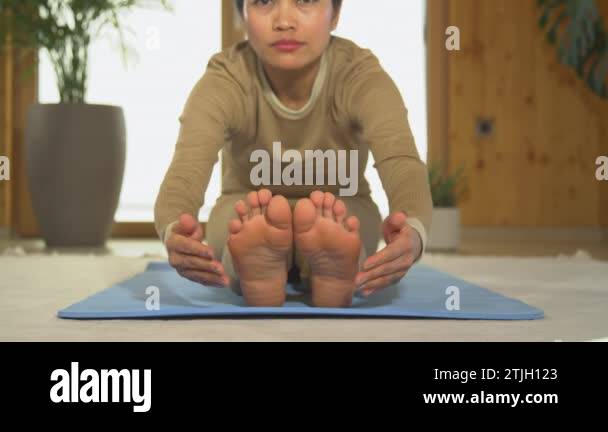 PORTRAIT Pretty young Asian woman doing a sitting stretch, smiling into ...