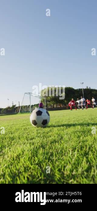 Vertical video of biracial football player on field kicking ball. Male ...