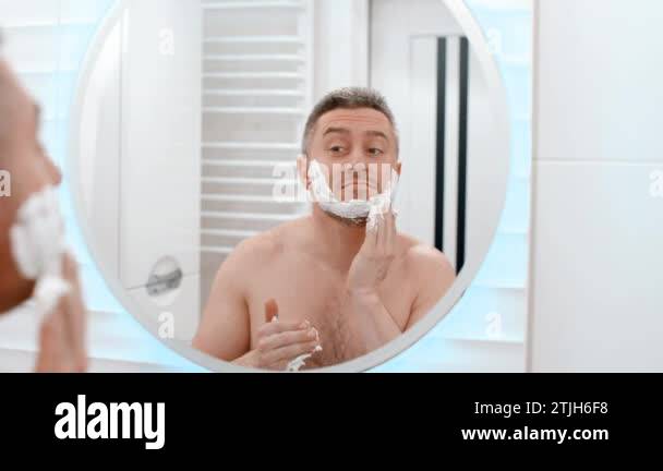Man, face in mirror and shaving cream, hygiene and grooming with beauty and skincare in morning ...