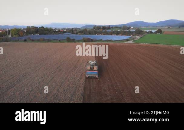 Tractor with harrow system plowing ground on cultivated farm field ...