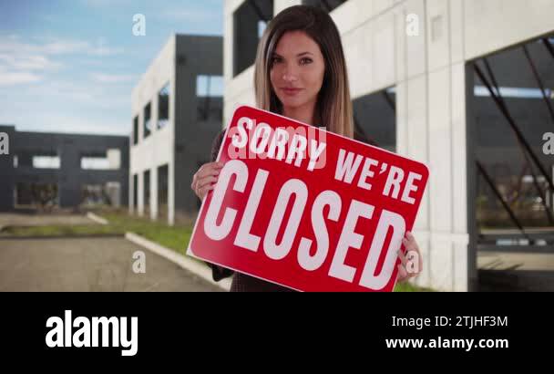 Woman holding Closed sign outside some abandoned buildings. Female ...