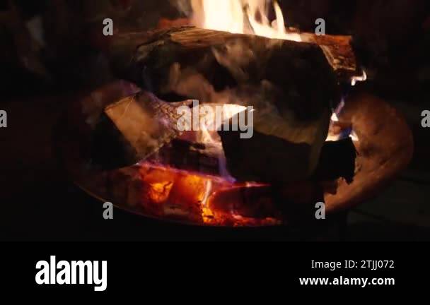 Firewood burns in a fire close-up, people around the fire warm their ...