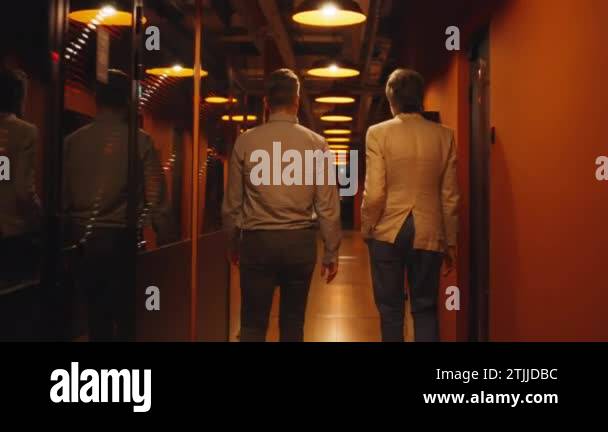 Male colleagues in suits walking down in hallway together, talking ...