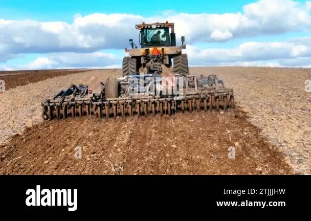 Rear view of tractor and plow plowing and preparing soil for sowing. A tractor prepares soil for ...