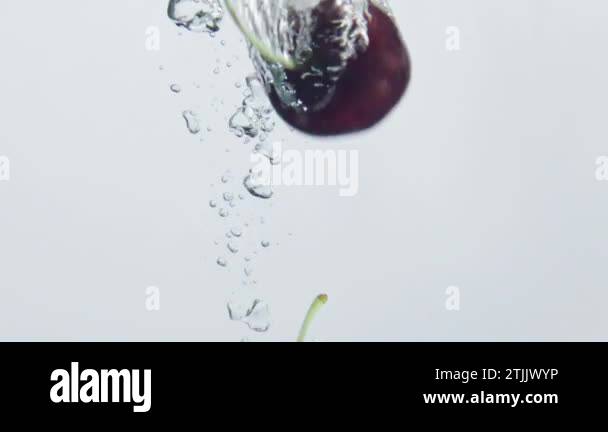Ripe tasty cherries falling into clear water making splashes bubbles at ...