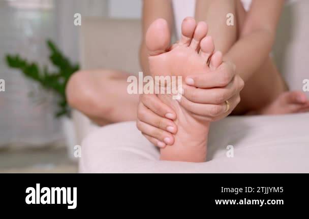Foot pain, Asian woman sitting on sofa feeling pain in her foot at home ...