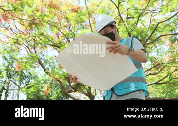 Masked male architect looks at the blueprints of a garden area that ...