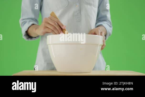 A young black woman stirs a bowl with a wooden spoon on green screen ...