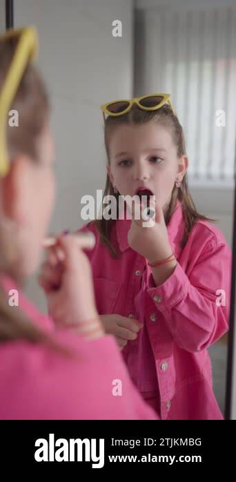 Little girl putting on lipstick in front of the mirror. Child putting ...