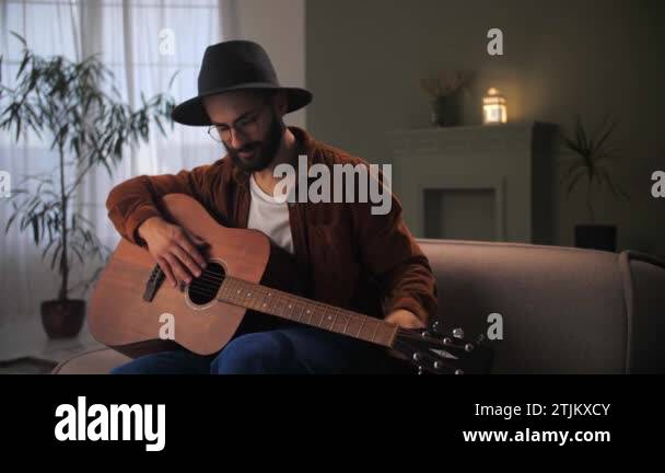 Man playing acoustic guitar sitting at sofa in home interior.Young ...