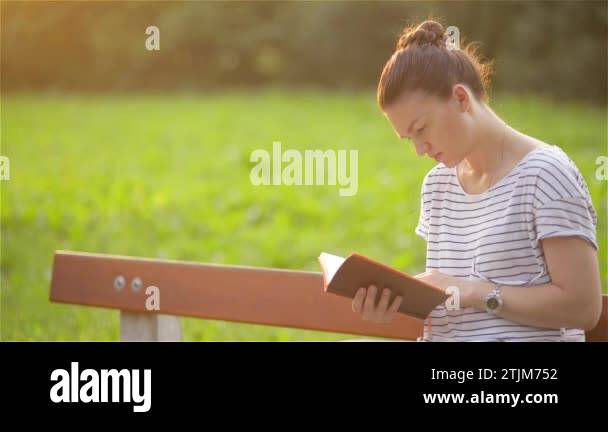 Beautiful Woman sitting on a bench in the park and reading a book ...