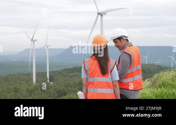 Male and female engineers working on a wind farm atop a hill or mountain in the rural ...