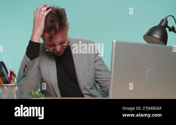 Displeased business man sits at office desk rubbing temples to cure headache problem, suffering ...