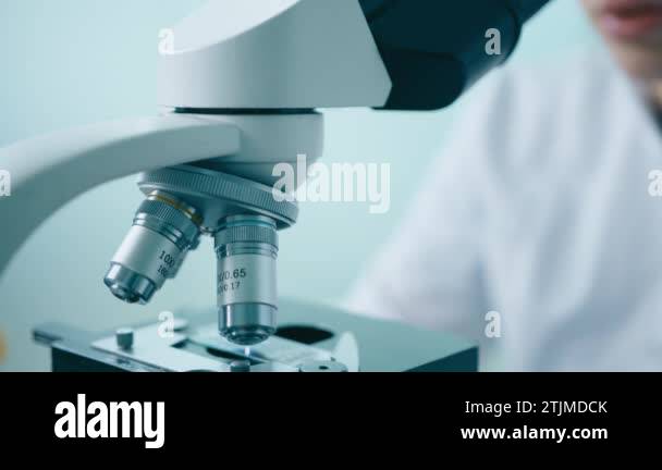 Close up microbiologist in white medical uniform looks under microscope ...