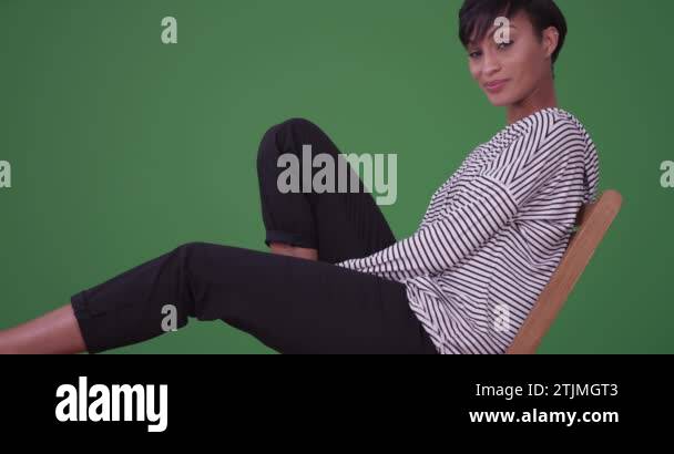 Black woman relaxing on a patio chair while looking at camera on green ...