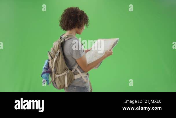 Black millennial girl reads a map while her hiking backpack is on green ...