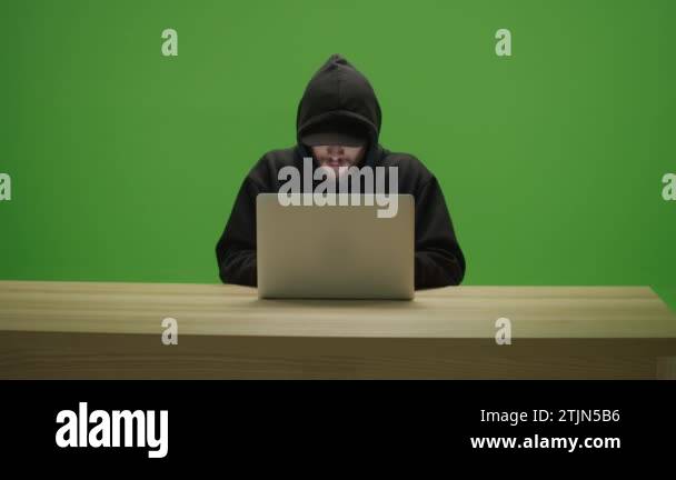 Unrecognizable Man Hacker Wearing Sweatshirt With Hood And Cap Typing On Laptop Computer