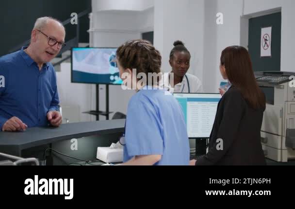 Diverse medical team working at hospital reception desk, nurse helping old patient with report ...