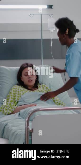 Vertical video: Asisstant with black skin arrange sick woman bed during ...