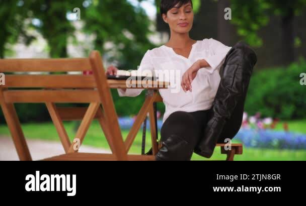 Attractive black woman poses sitting down outside in a green garden ...