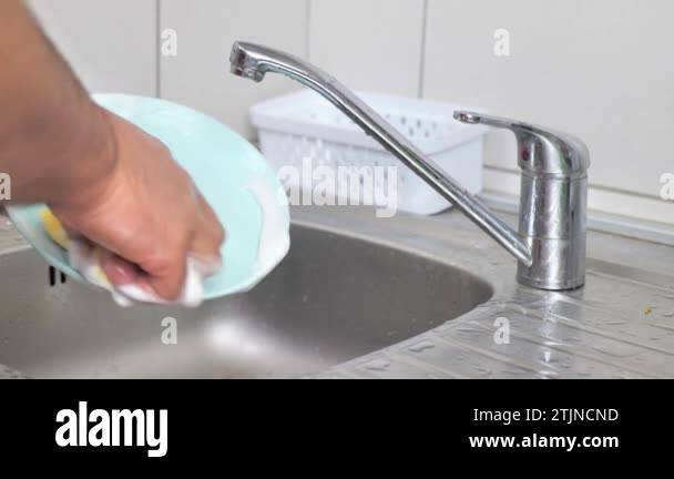 A young man washes dishes at home with soap and a sponge. The guy ...