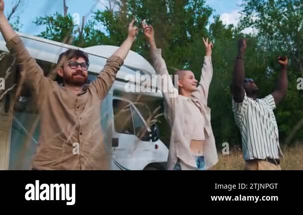 Three friends outside camper van jumping with raised arms in ...