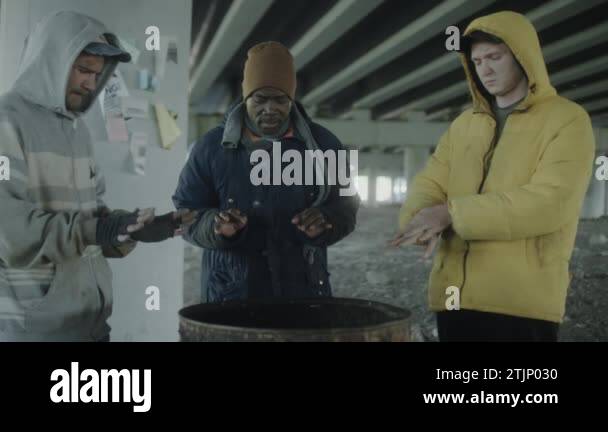 Company of multiethnic homeless men warming their hands over fire ...