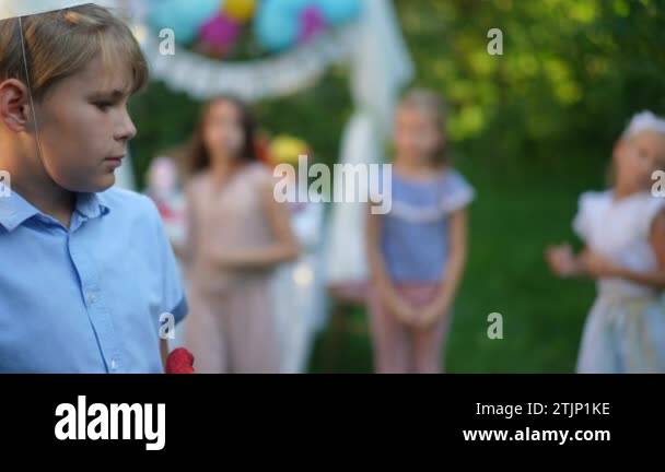 Bored sad Caucasian birthday boy looking back at blurred cheerful girls ...