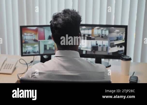 Back view of security guard monitoring surveillance cameras at ...