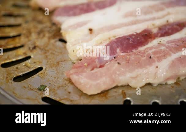 Close up shot of hand cooking Korean grilled pork belly meat on iron ...
