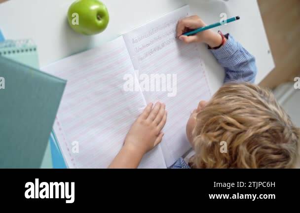 Elementary school student boy or girl writing letters, studying at desk ...