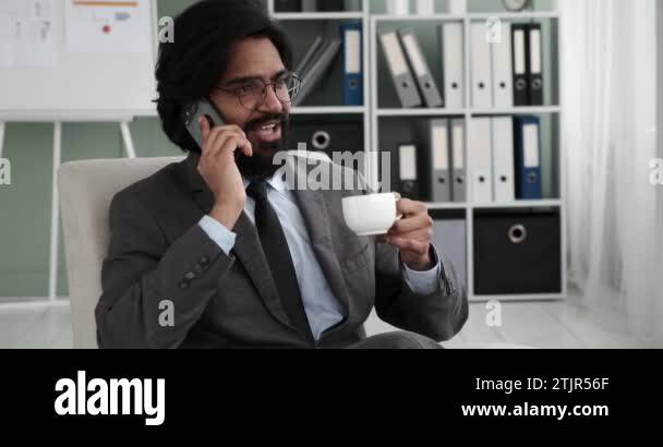 An Indian businessman is sitting in a comfortable armchair, talking on ...
