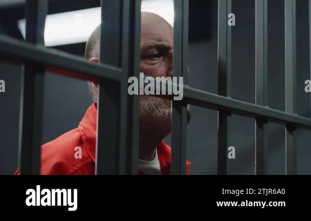 Face close up of elderly prisoner in orange uniform standing behind ...