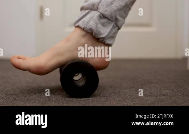 Woman doing flatfoot correction gymnastic exercise using massage roller ...